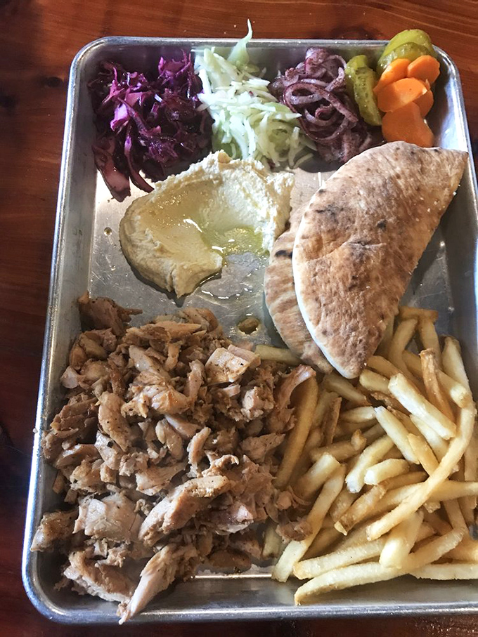 A festival of textures and flavors &ndash; succulent meat, vibrant vegetables, and creamy hummus sharing space on a metal tray like old friends at a reunion.