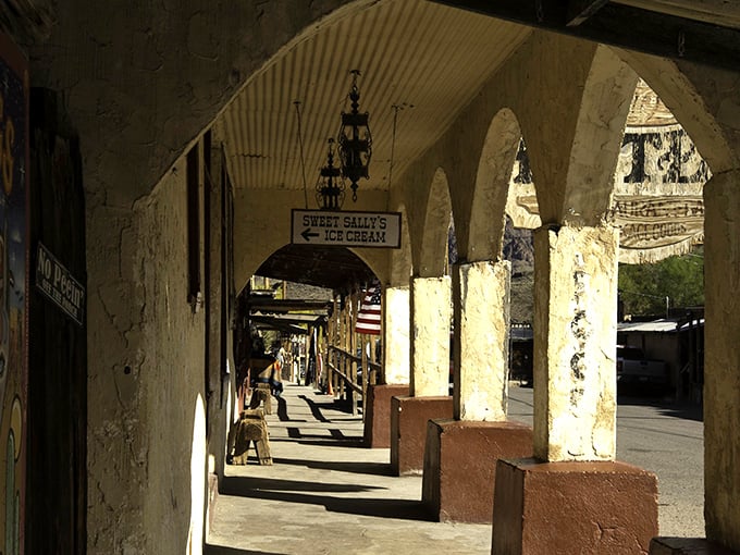 Sunlight creates dramatic shadows through the historic arcade, where Sweet Sally's Ice Cream sign promises cool relief from the Arizona heat.