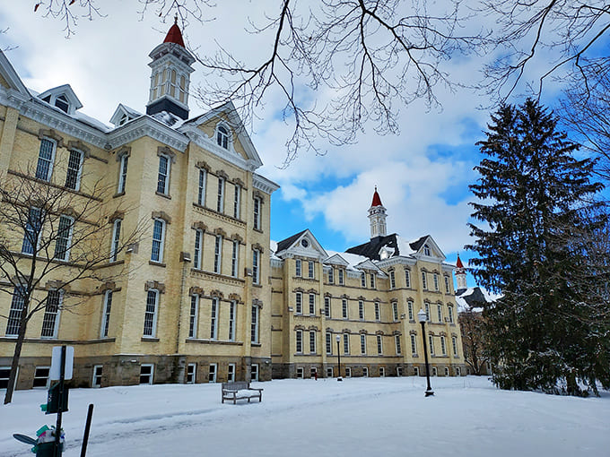 Winter transforms the asylum grounds into a snow-globe scene, the yellow brick buildings standing in stark contrast to the pristine white landscape.