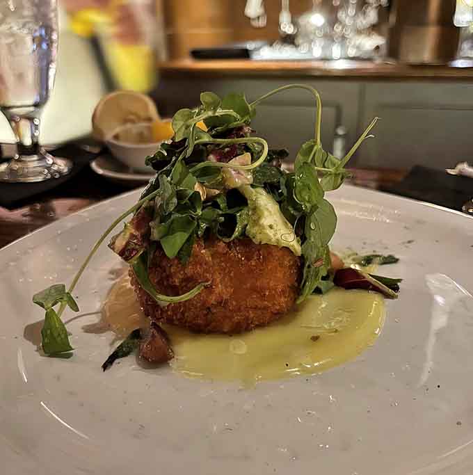 The crab cake arrives like a golden crown atop a pool of sunshine-yellow sauce, packed with sweet lump meat and barely enough binder to remind you it's not just a pile of crab.
