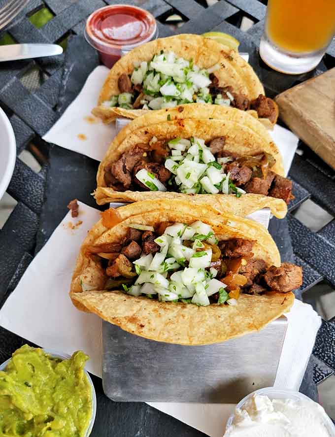 The holy trinity of taco perfection: seasoned steak, fresh toppings, and warm tortillas, accompanied by a cold beer that makes Monday feel like Friday.