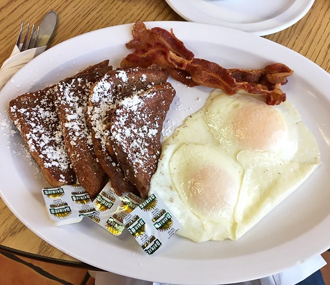 French toast dusted with powdered sugar shares the plate with crispy bacon and sunny-side-up eggs &ndash; the breakfast trifecta of sweet, salty, and savory.
