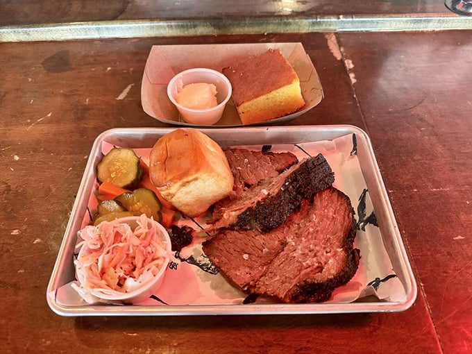 The brisket plate arrives like a carnivore's dream &ndash; tender smoked meat accompanied by pickles, slaw, and cornbread for the perfect balance.