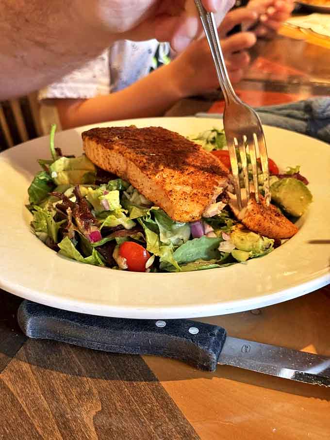 Perfectly seared salmon perches atop a garden of greens, a protein-packed oasis for those navigating around heavier menu options.