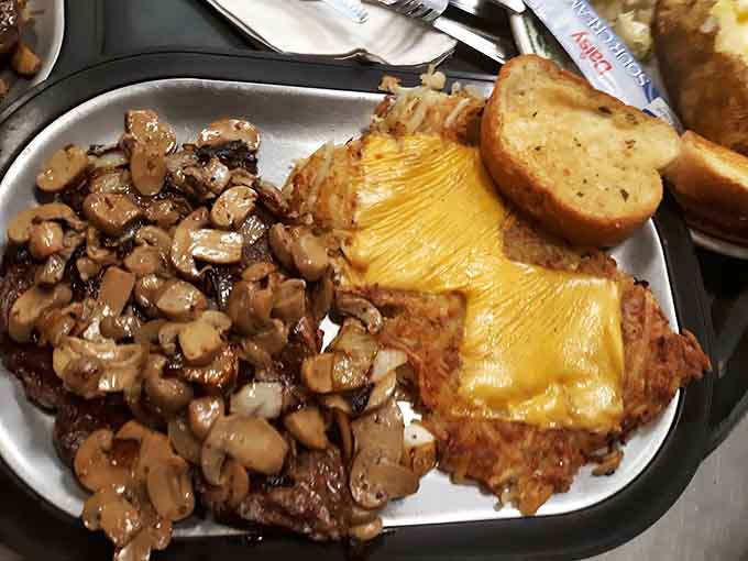 This ribeye wears its mushroom topping like a crown, sitting pretty next to garlic bread that's basically edible happiness on a plate.
