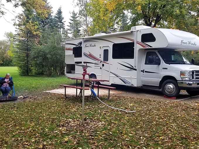 That RV is living its best life, parked under trees that provide shade, beauty, and probably a few extra leaves to sweep off the roof.