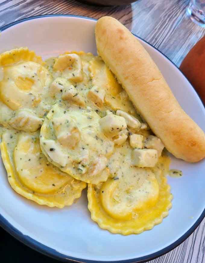 Tender ravioli swimming in creamy sauce with a breadstick sidekick, ready to comfort your soul one delicious bite at a time.