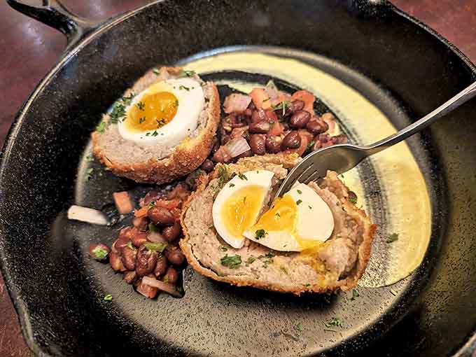 Scotch eggs done right &ndash; perfectly soft-boiled centers encased in savory sausage, fried to golden perfection and served with beans for a hearty starter.