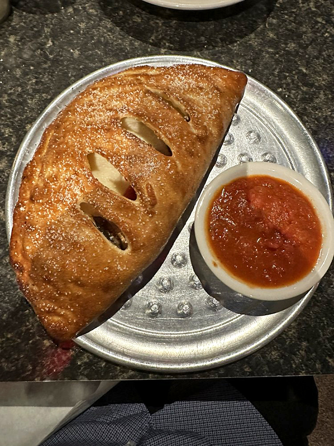 The calzone: a golden-brown pocket of joy that, when cut open, releases a steam cloud so aromatic you might momentarily forget your name.