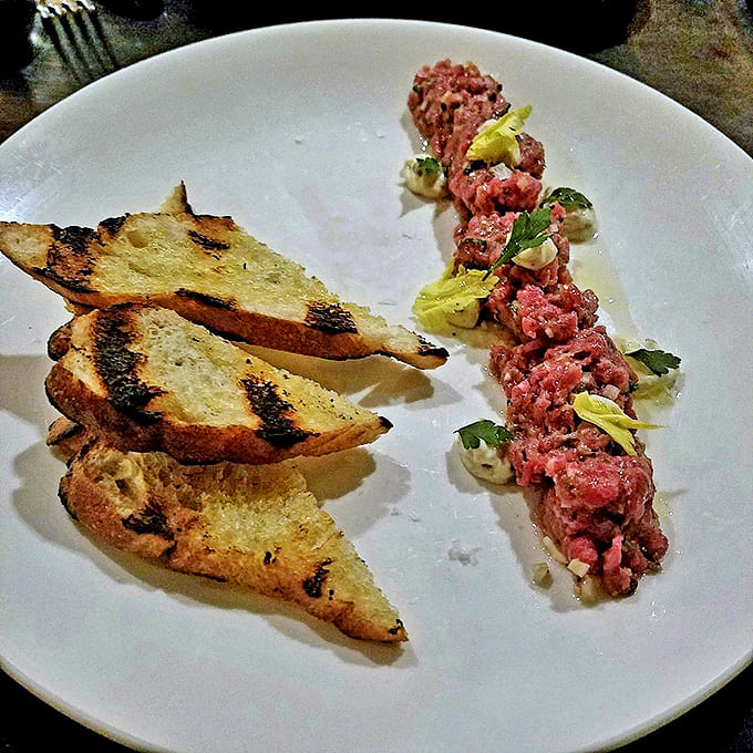 Steak Tartare with Crostini: A study in contrasts &ndash; delicate raw beef meets crispy grilled bread. The arrangement suggests careful plating that's both artistic and practical.