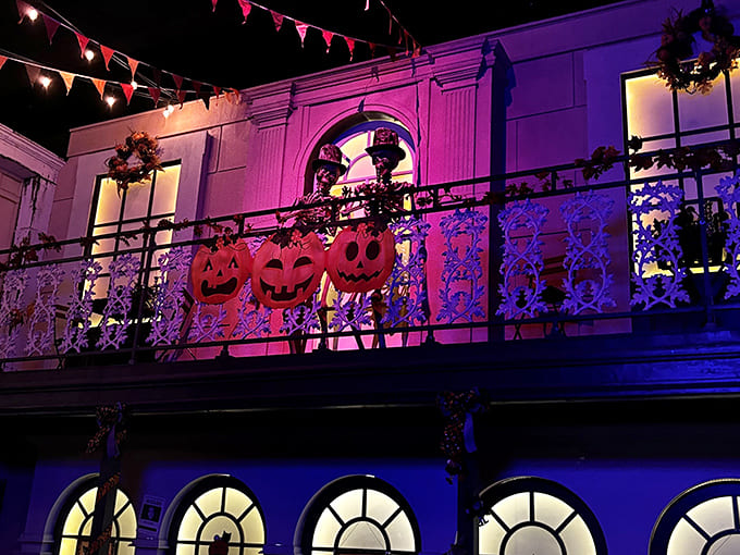 Jack-o'-lanterns grin mischievously from the balcony, their carved faces illuminated by an otherworldly purple glow.
