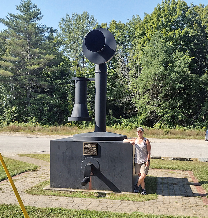 A visitor poses beside the monument, offering scale perspective that emphasizes just how massive this telephone tribute truly is.