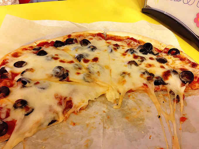 Pizza perfection with stretchy cheese and black olives scattered like treasures across the surface&mdash;an unexpected diner specialty worth celebrating.