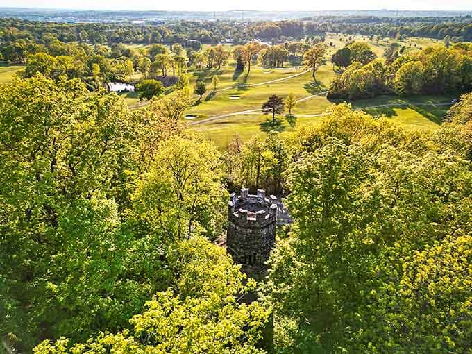 Bird's-eye perspective reveals the tower's strategic hilltop position, a stone sentinel standing guard over emerald canopy and winding fairways.