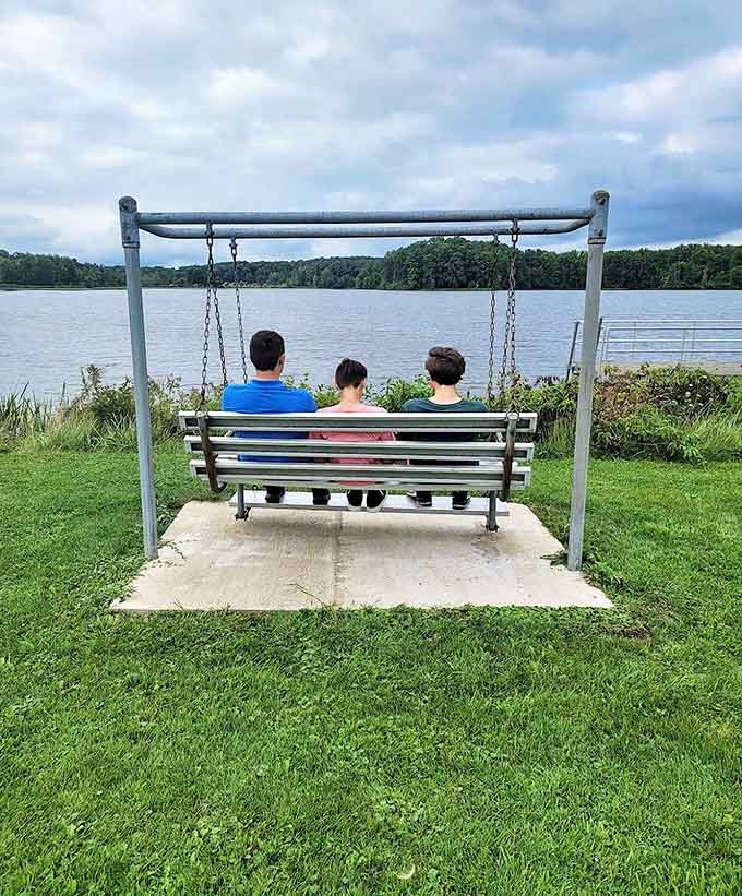 Three visitors share a moment of tranquility on the lakeside swing, watching ripples dance across the water's surface.
