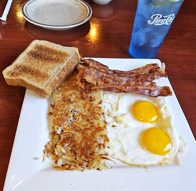 Breakfast perfection: crispy hash browns, eggs sunny enough to brighten your morning, and bacon that's worth setting the alarm for.