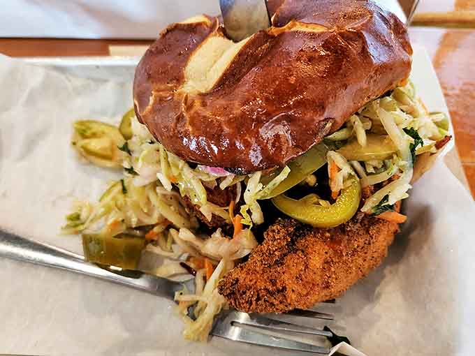 This sandwich masterpiece stacks crispy chicken, tangy slaw, and pickles on a glossy pretzel bun &ndash; a towering achievement in handheld deliciousness.