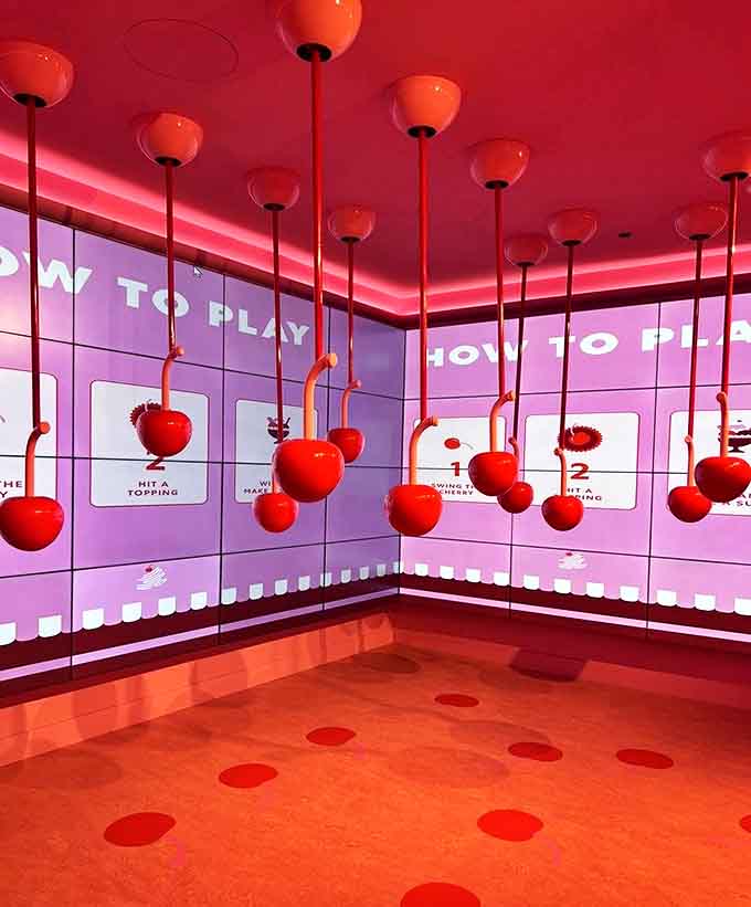 Hanging cherries invite playful interaction in this game room, where visitors can test their skills while bathed in a rosy glow.