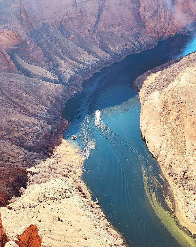 A boat creates ripples through emerald waters below, offering scale to the massive canyon walls that tower overhead.