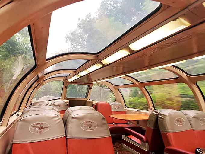 Vintage train seats with "Silver Lariat" headrest covers offer passengers comfort with a view, beneath windows that frame the passing scenery.