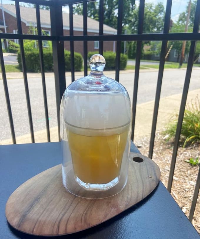 The Pineapple Express cocktail arrives under a glass cloche like a tropical vacation trapped in a very sophisticated snow globe.