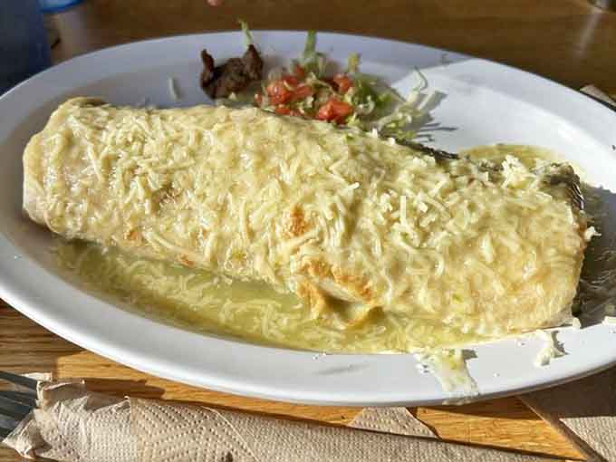 A wet burrito smothered in sauce and cheese, transforming a handheld meal into a fork-required feast that's worth every messy bite.