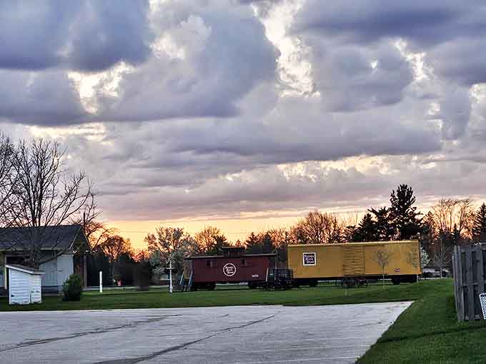 As dusk approaches, vintage train cars rest under dramatic clouds, monuments to an era when the railroad's whistle meant connection to the world.