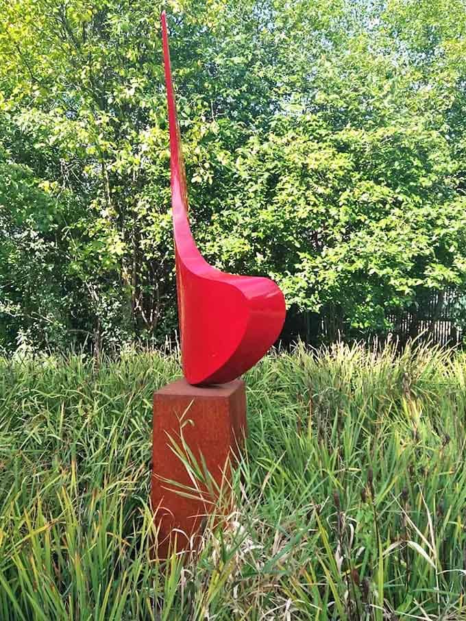 A scarlet sail catches imaginary wind, its bold color a striking exclamation point against the garden's more subdued palette.