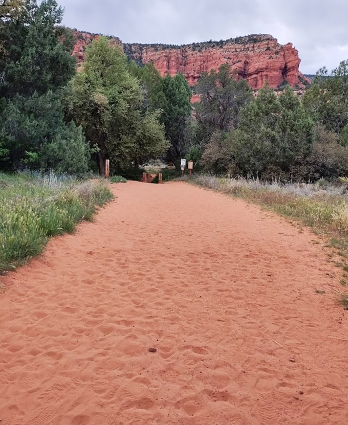 The sandy trail beckons with promises of discovery, its rusty hue matching the magnificent cliffs that frame the path.