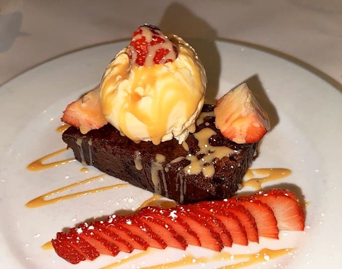 Rich chocolate brownie topped with ice cream and fresh strawberries, because every great seafood feast deserves a sweet ending.