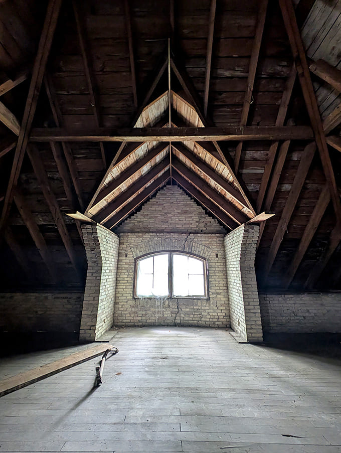Sunlight streams through attic windows, illuminating century-old wooden beams in spaces that once stored patients' belongings and now await new purpose.
