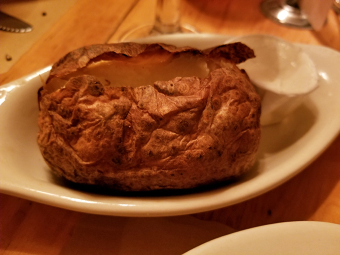 The baked potato arrives like a rustic treasure, its skin crisp and interior fluffy enough to create the perfect vehicle for butter and sour cream.