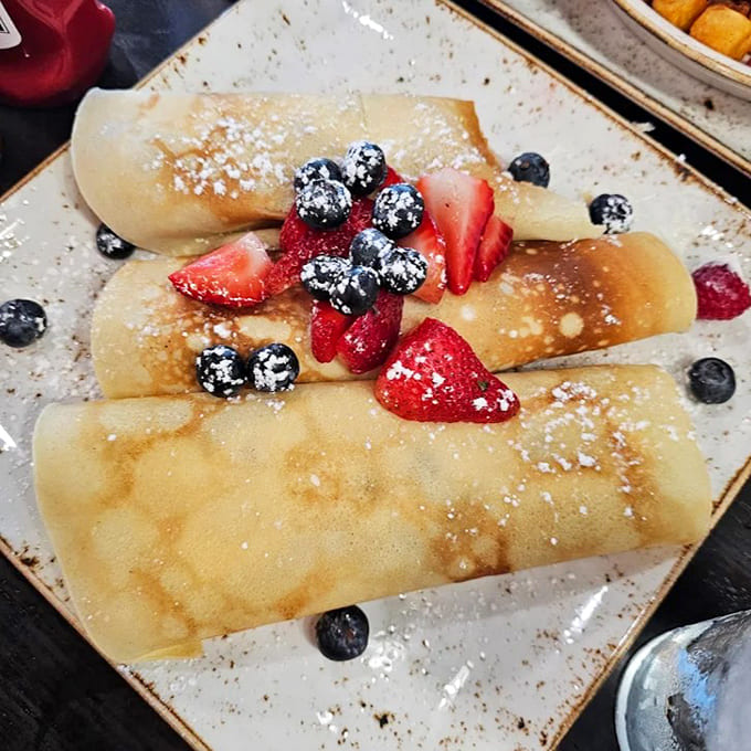 These delicate crepes cradle fresh berries and powdered sugar &ndash; proof that sometimes the simplest pleasures are the most satisfying.