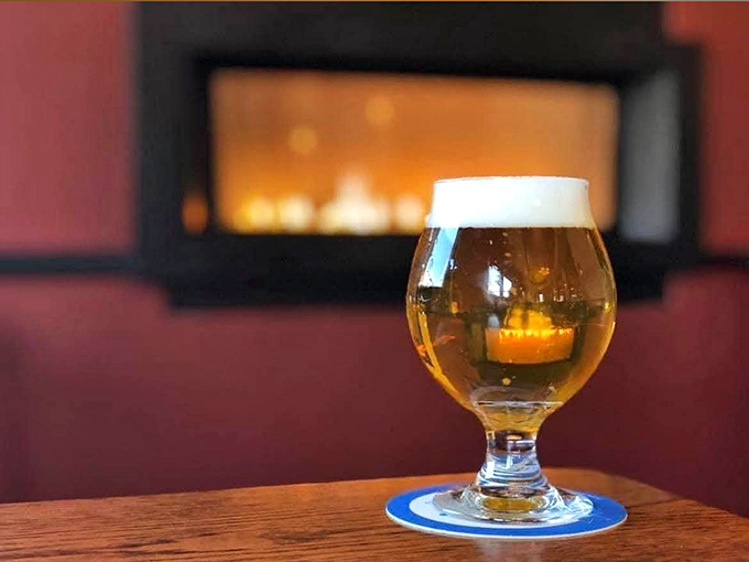 Amber beer glows like liquid gold against the fireplace backdrop &ndash; the perfect companion for Vermont's chilly evenings.