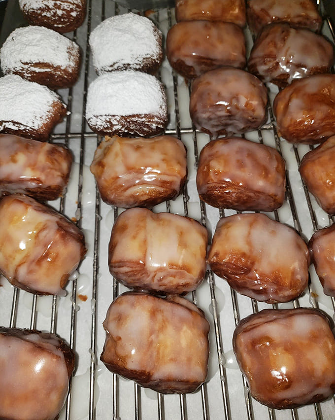 Fresh beignets lined up like little pillows of fried dough happiness, ready to dust your shirt with powdered sugar and your day with joy.