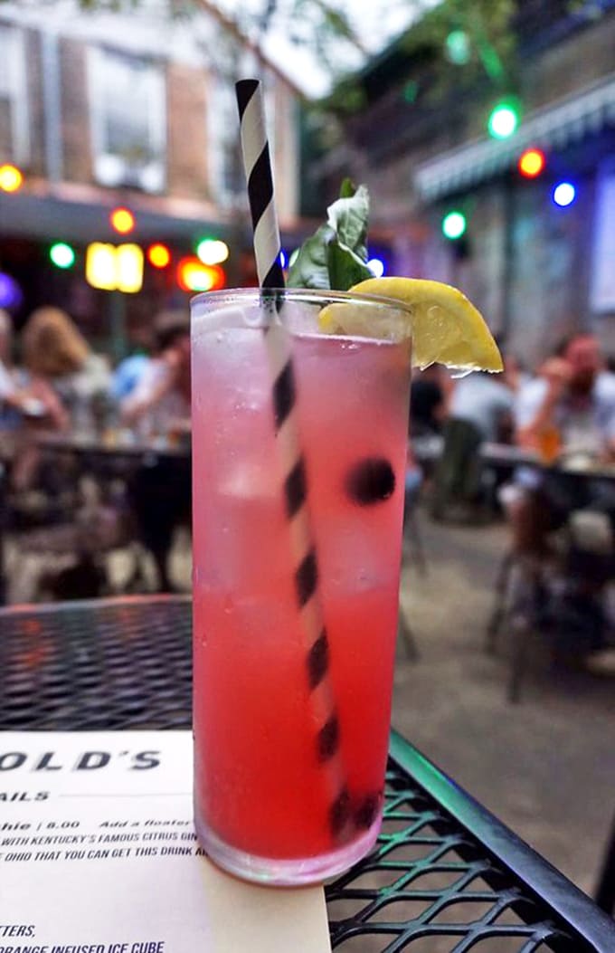 A blueberry lemonade catches the glow of courtyard lights, its striped straw and lemon garnish promising refreshment with a hint of Cincinnati spirit.