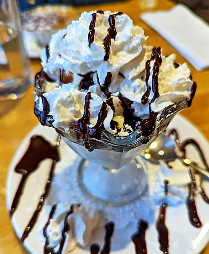 This hot fudge sundae channels serious vintage soda fountain energy with its whipped cream peaks and chocolate drizzle artistry.