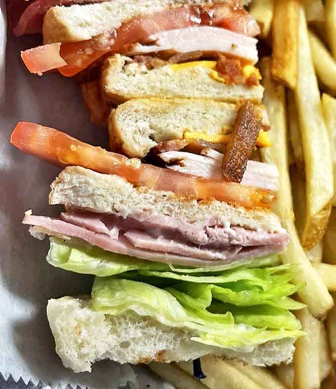 This club sandwich towers with layers of meat, cheese, and vegetables, requiring serious architectural planning to eat.
