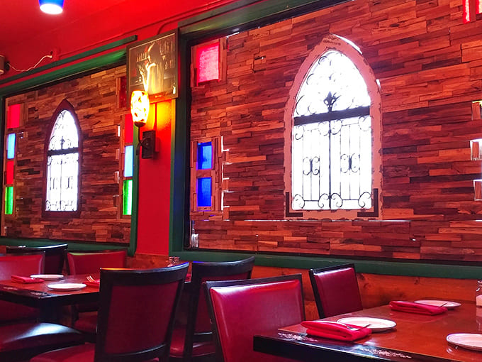 Red walls and decorative arched windows create intimate dining spaces where conversations flow as smoothly as the wine and every table feels special.