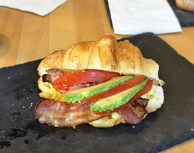 Breakfast sandwich artistry: Avocado, tomato, and bacon create a colorful symphony of flavors inside a perfectly flaky croissant.