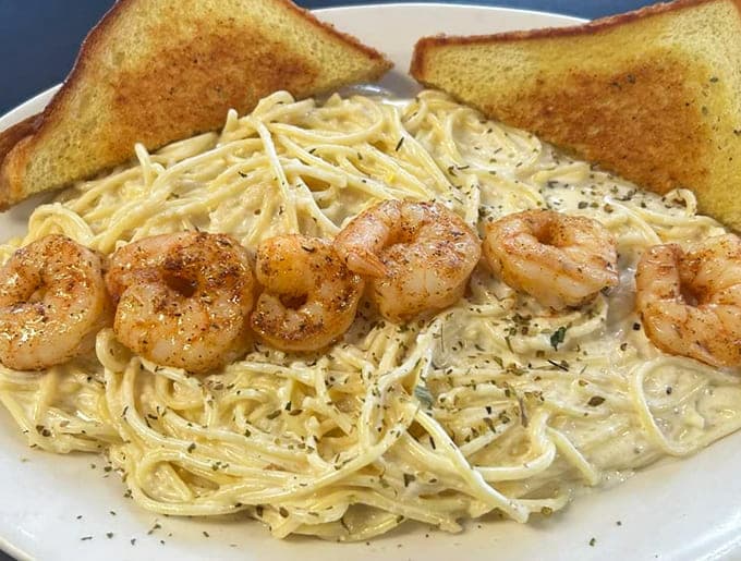 Plump shrimp nestled atop creamy alfredo pasta with buttery garlic toast &ndash; proof that simple ingredients become extraordinary in the right hands.