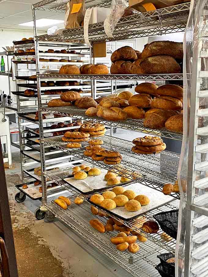 Behind-the-scenes bread paradise where the magic happens. Those racks of freshly baked goodness are basically a carbohydrate art gallery.