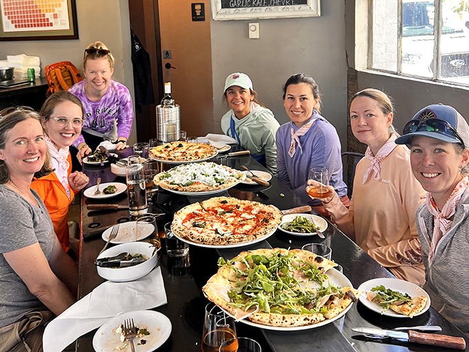 Happy diners sharing multiple pizzas &ndash; the best way to experience Pizzicletta's menu is with friends who don't mind swapping slices.