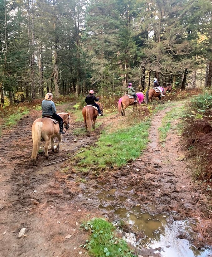 Riders navigate a muddy section of trail, their horses stepping carefully while fallen leaves create natural mosaics in puddles.