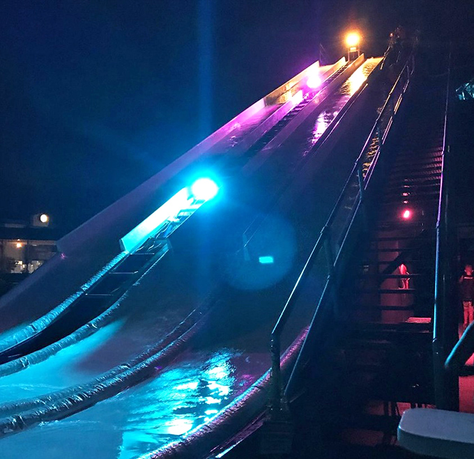 Night transforms the slide into a neon playground, where adults reclaim their youth under the cover of darkness.