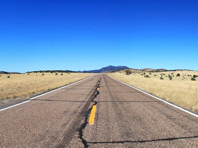The open road stretches endlessly through golden grasslands, where mountains stand guard like ancient sentinels against the Arizona sky.