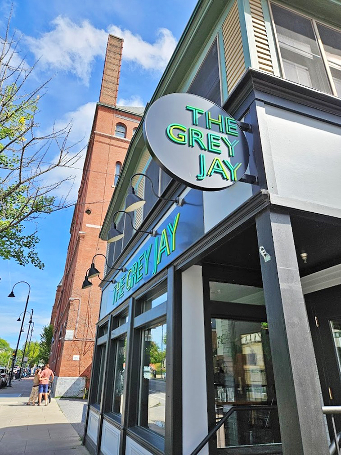 The Grey Jay's sleek neon sign glows like a beacon of culinary promise against Burlington's historic brick backdrop.