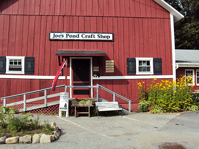 A classic red Vermont barn with white trim houses Joe's Pond Craft Shop, where yellow wildflowers welcome visitors like nature's own welcome committee.
