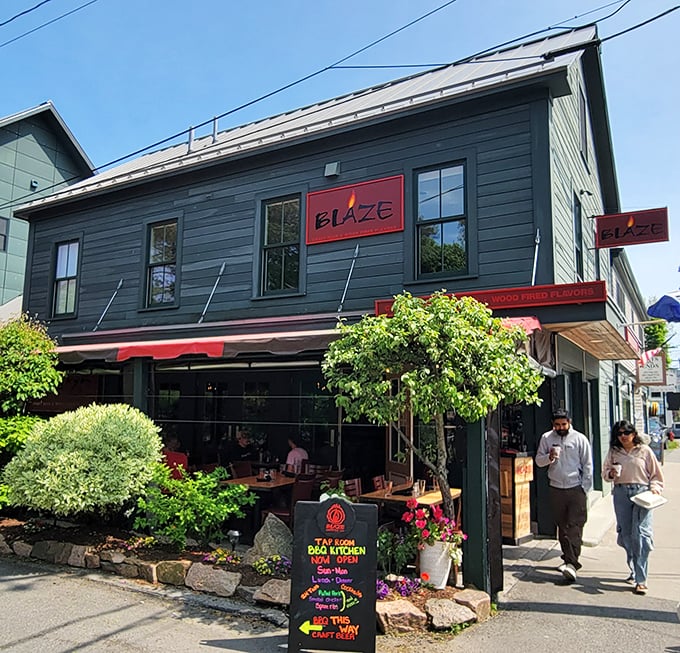 A forest-green facade with bold red accents welcomes visitors to Blaze, where hanging flower baskets and a chalkboard sign promise wood-fired delights within. Photo credit: R Houseman