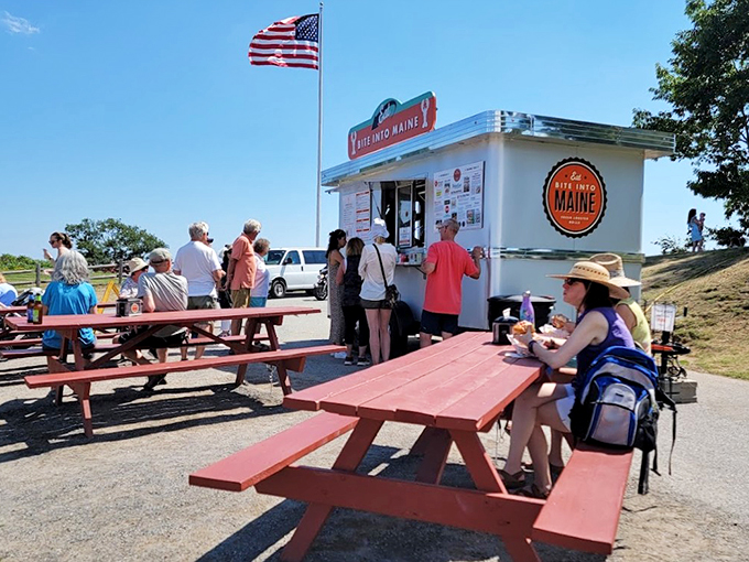A perfect Maine summer day unfolds at Fort Williams Park, where red picnic tables and an American flag frame this beloved lobster destination.